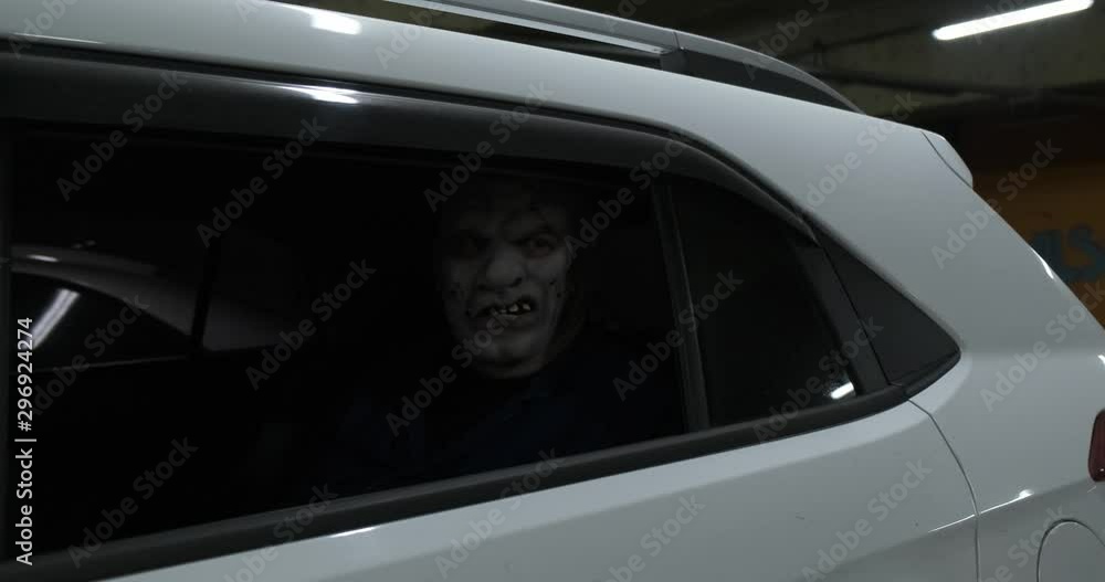 In back seat of white car sits maniac in white scary mask, wry smile ...