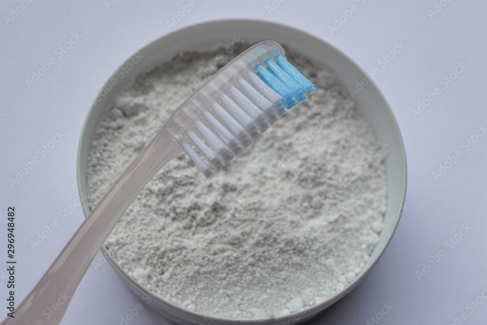 Close-up of a white toothbrush with blue bristles and an open round jar ...