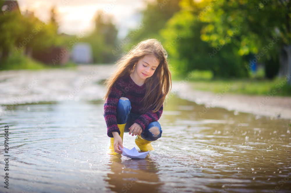girl in yellow sopog plays in a puddle in a small boat, children's fun ...