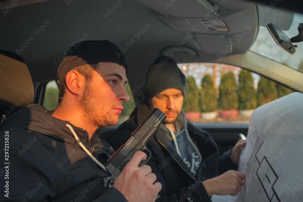 Two robbers sitting inside a car with guns looking at the blueprint of ...