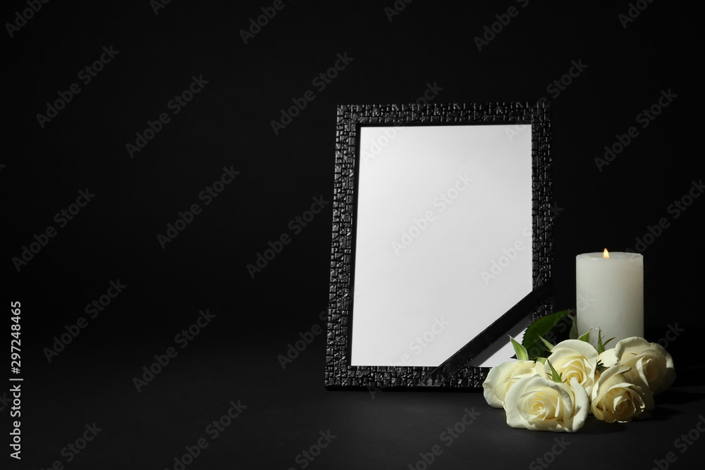 Funeral photo frame with ribbon, white roses and candle on dark table ...