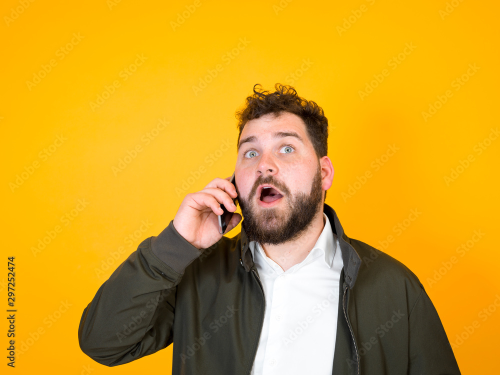 cool man with smartphone, black beard and black hair is posing in front ...