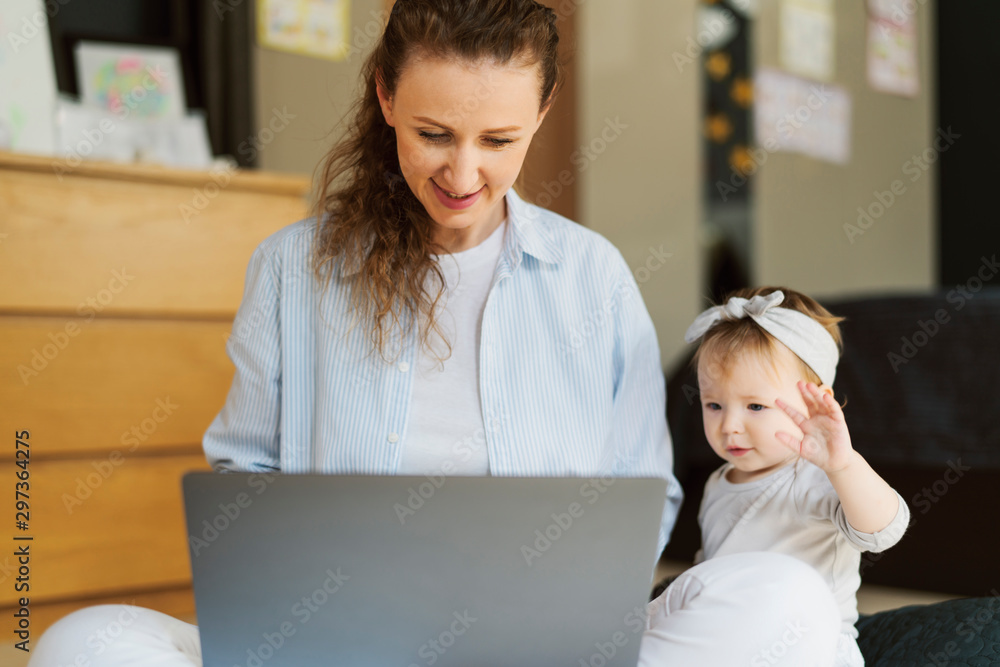 Young woman typing on laptop, little daughter sitting near and playing ...