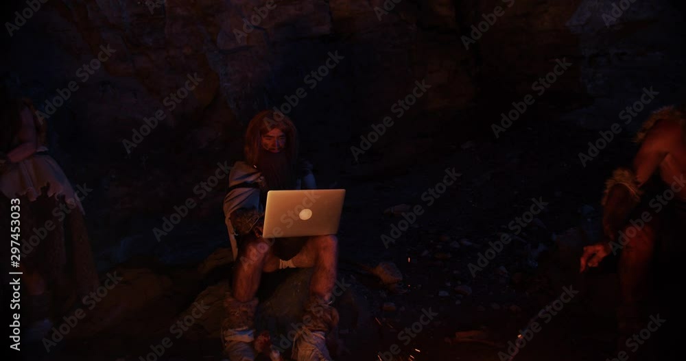 In dark neanderthals wearing animal skin use tablet computer sitting by ...