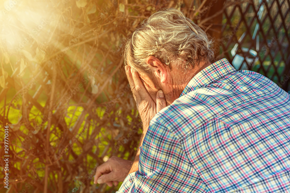 Older man worried and supporting his head with his hand in sun rays ...