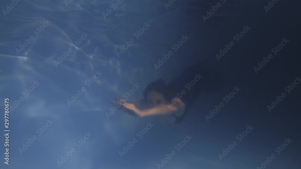 Fit woman in blue dress is diving and swimming underwater in the pool ...