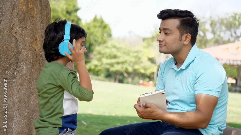 Indian father and son using a tablet with blue headphones while ...