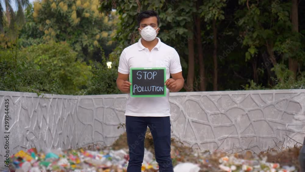 Indian man showing a slate of "Stop Pollution" text with garbage dump ...