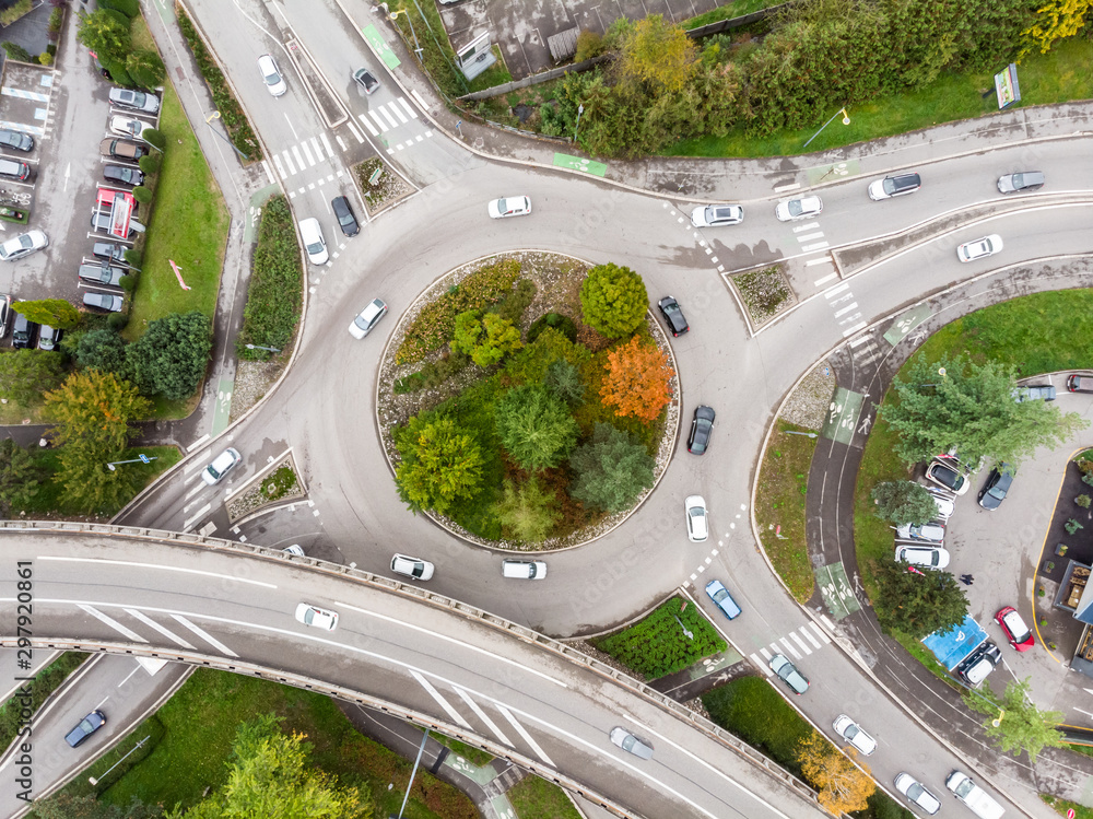 Roundabout road intersection with vehicle traffic and green trees ...