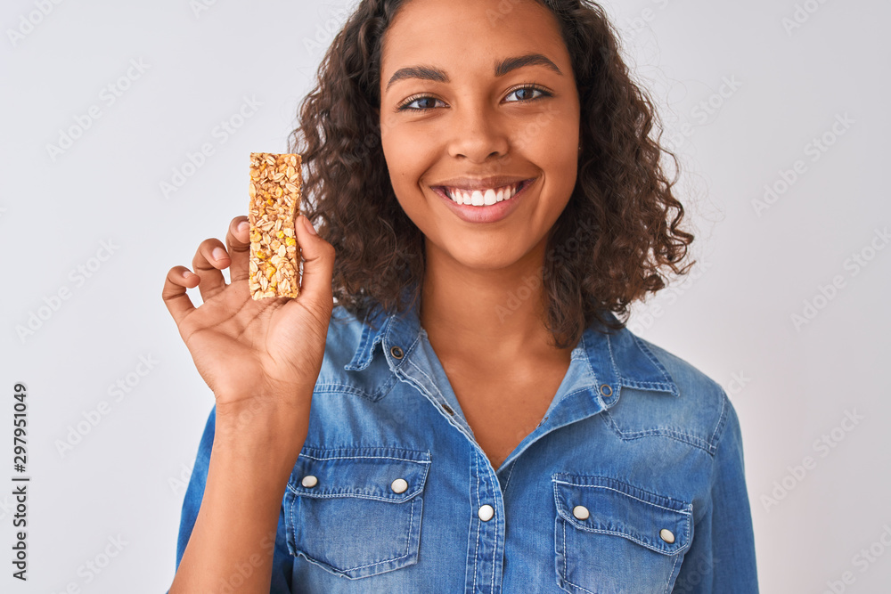 Young brazilian woman eating granola bar standing over isolated white ...
