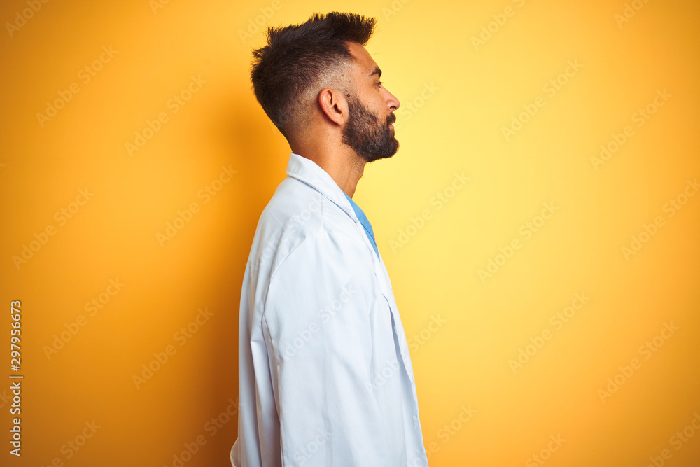 Young indian doctor man standing over isolated yellow background ...