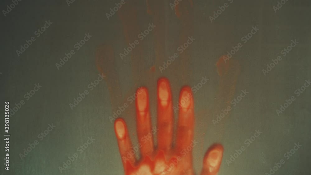 A bloodied hand descends down a glass partition in the bathroom under ...