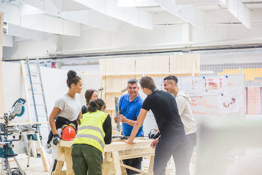 Male instructor teaching about level to trainees standing at workbench ...