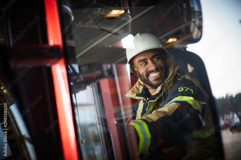 Smiling firefighter sitting in fire engine seen through glass window ...