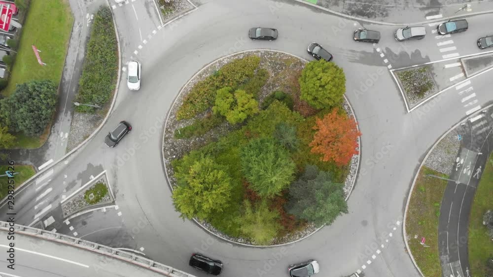 Roundabout road intersection with vehicle traffic and green trees ...