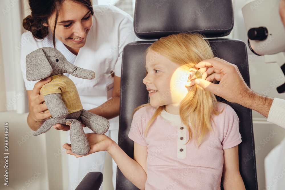 Nurse distracting child with toy while doctor using surgical microscope ...