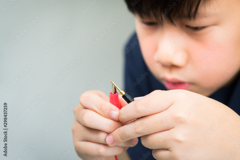 Smart looking Asian boy connecting a crocodile clip with multimeter ...