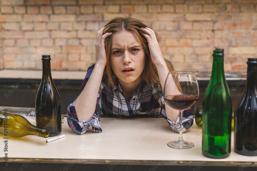Young sad and wasted alcoholic woman sitting at kitchen couch drinking ...