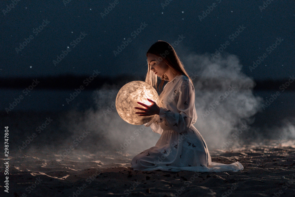Beautiful young girl on a night beach with sand and stars holds the ...