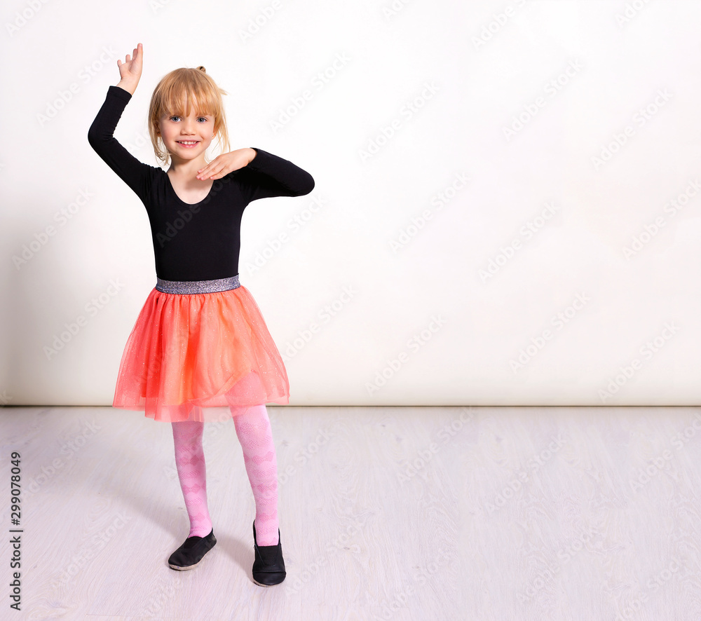 Little blonde ballerina girl posing in dance club with wooden floor and ...