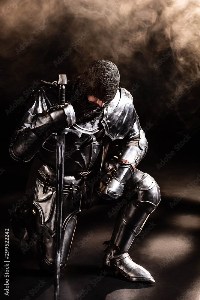 handsome knight in armor holding sword and bend knee on black ...