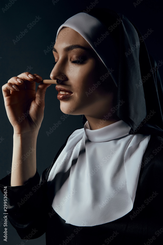 Close-up half-turn portrait of a nun, taking on a black background. She ...