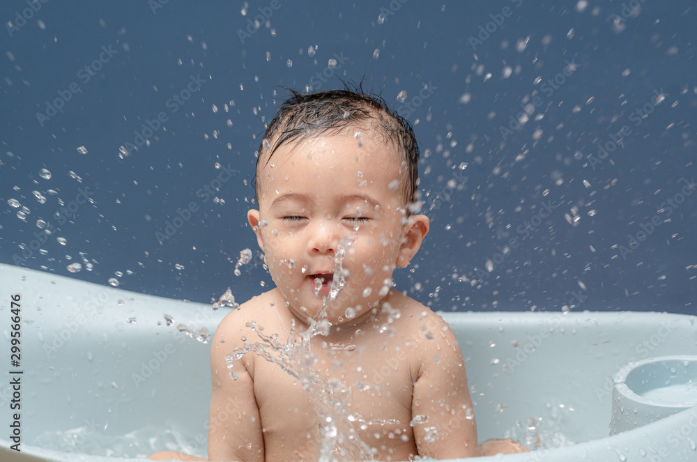 Cute baby boy bathes in a bathtub play and making splash water drops ...