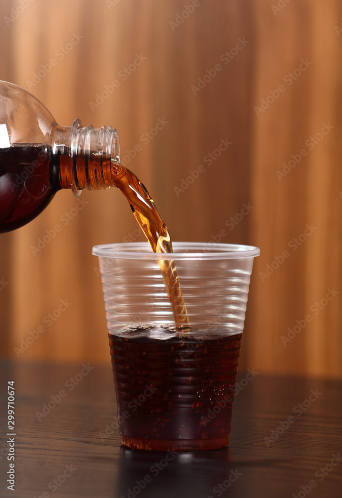 Pouring cola from bottle into plastic cup. Stock Photo | Adobe Stock