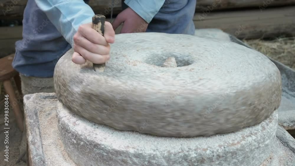 The ancient quern stone hand mill with grain. The man grinds the grain ...