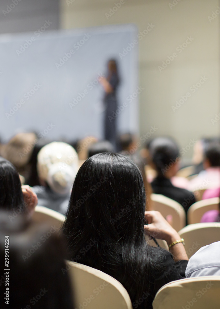 Audience watching a presentation. Female presenter on stage giving talk ...