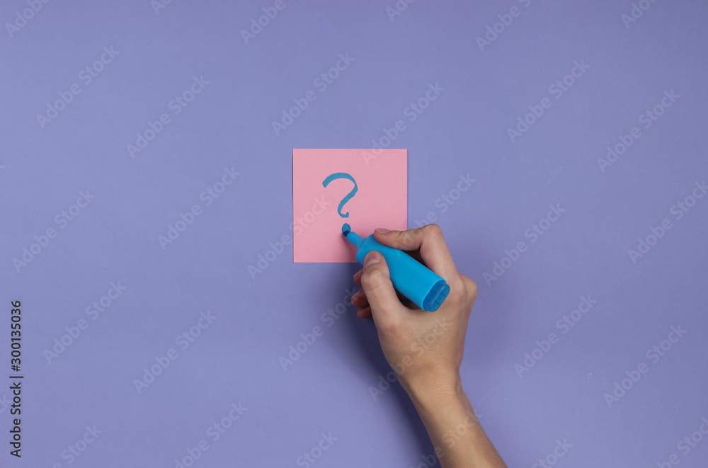 Female hand holds a blue felt-tip pen and draws question marks on memo ...