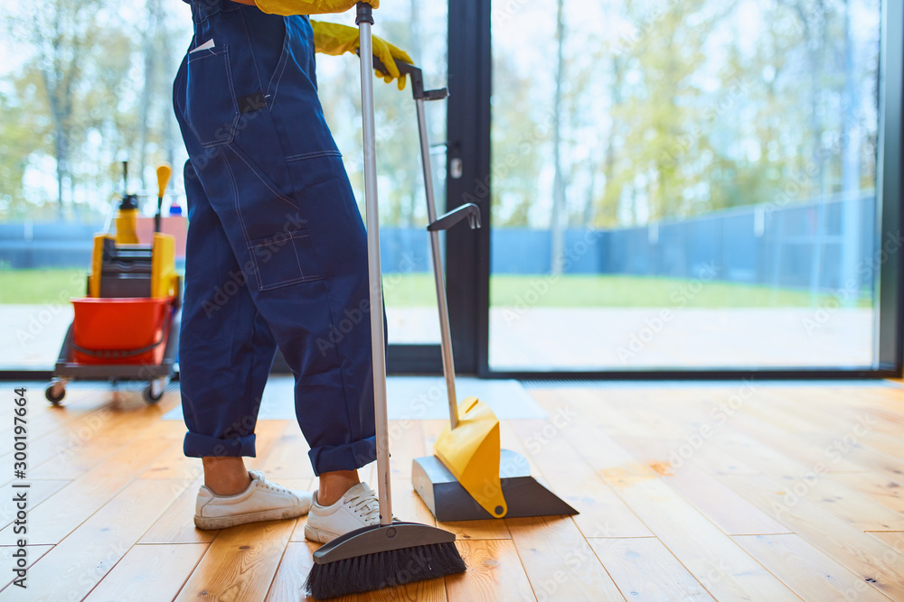 Side view on young cleaner sweeping the floor in living room, panoramic ...