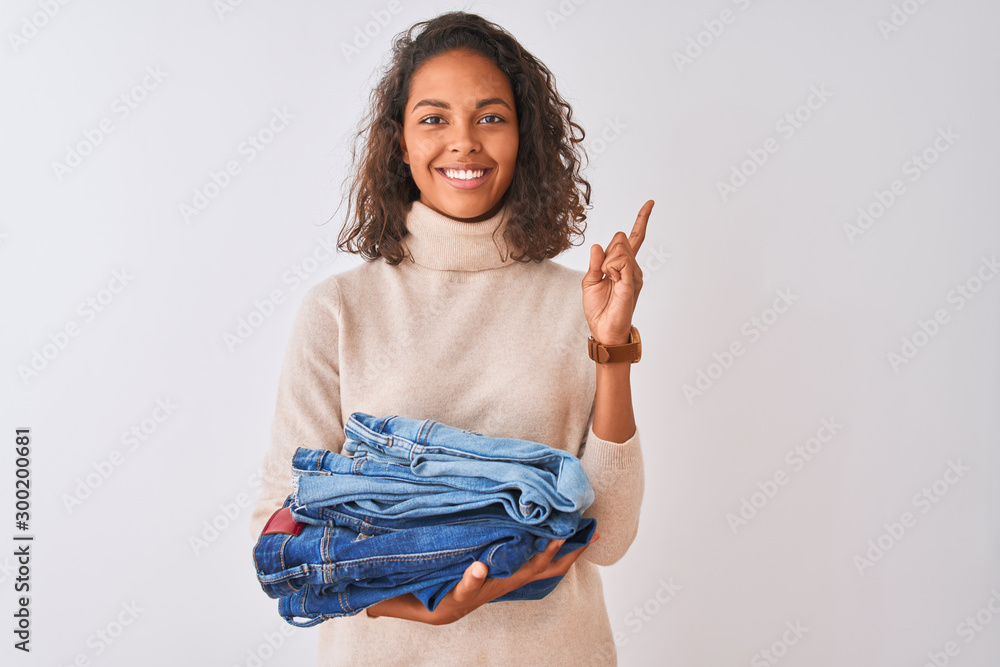 Young brazilian shopkeeper woman holding pile of jeans over isolated ...