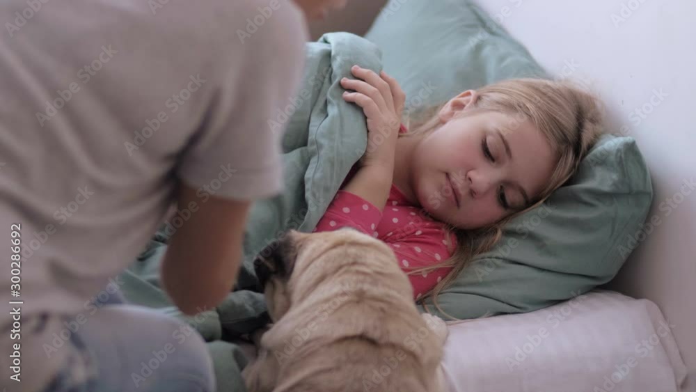 Mother caring for sick child lying in bed with flu measuring temperature using thermometer, girl ...