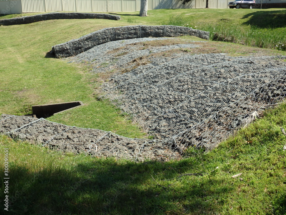 Stone walls under steel mesh creating a spillway for rain water flood ...
