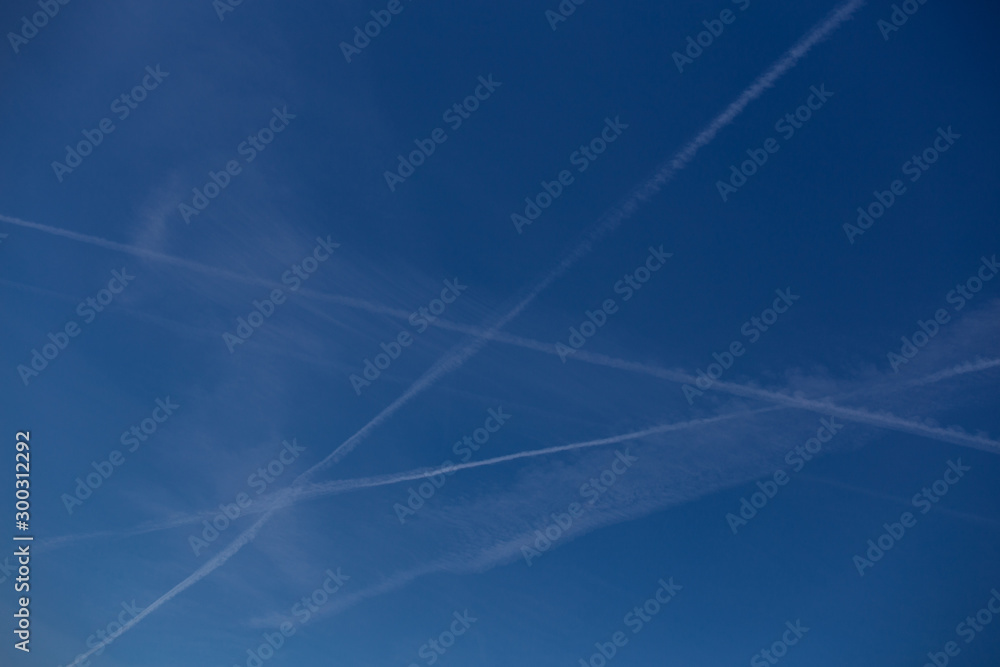 Blue sky with clouds, traces of airplanes draw diagonal lines in the ...