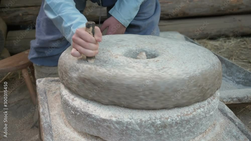 The ancient quern stone hand mill with grain. The man grinds the grain ...