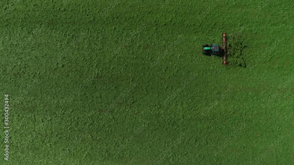 Aerial top-down view of green grass farm field with tractor raking ...