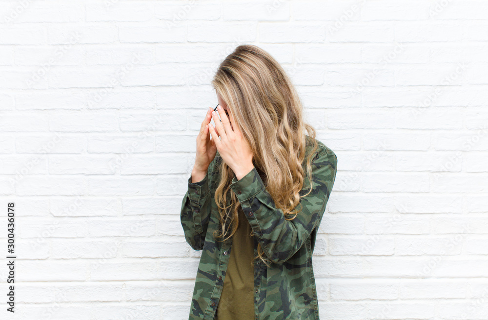 young blonde woman covering eyes with hands with a sad, frustrated look ...