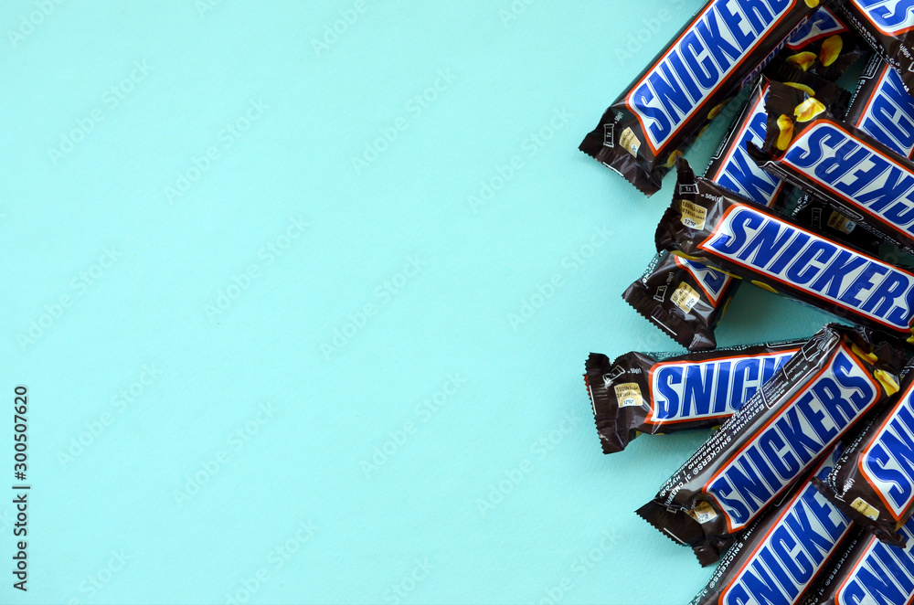 Many Snickers chocolate bars lies on pastel blue paper. Snickers bars ...