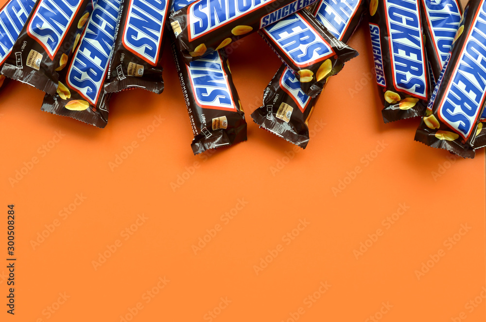 Many Snickers chocolate bars lies on pastel orange paper. Snickers bars ...