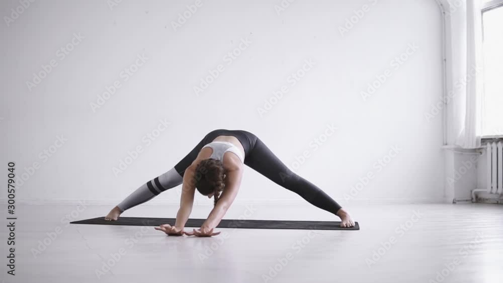 Flexible woman practice yoga postures standing in twine in white loft ...