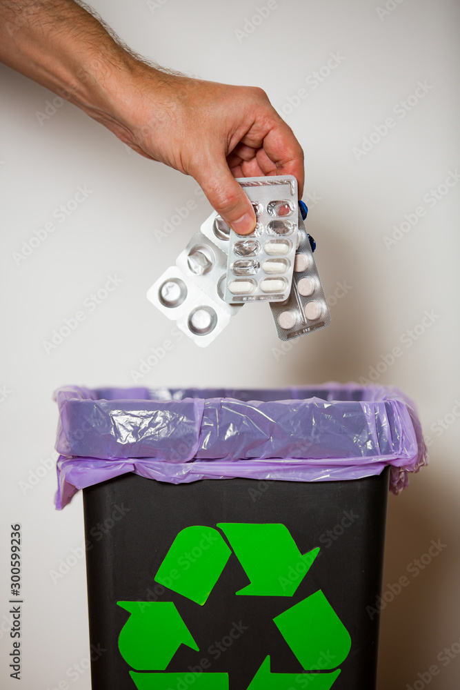 Hand putting expired medicine packages into bin with recycling sign for ...