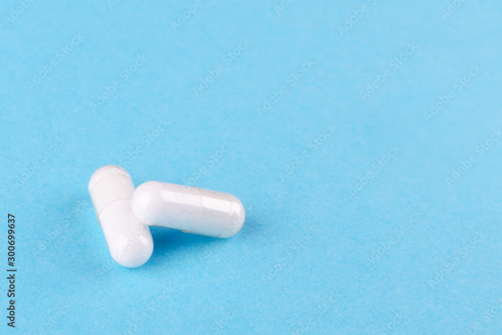 two white capsules of nutritional supplement on blue background with ...