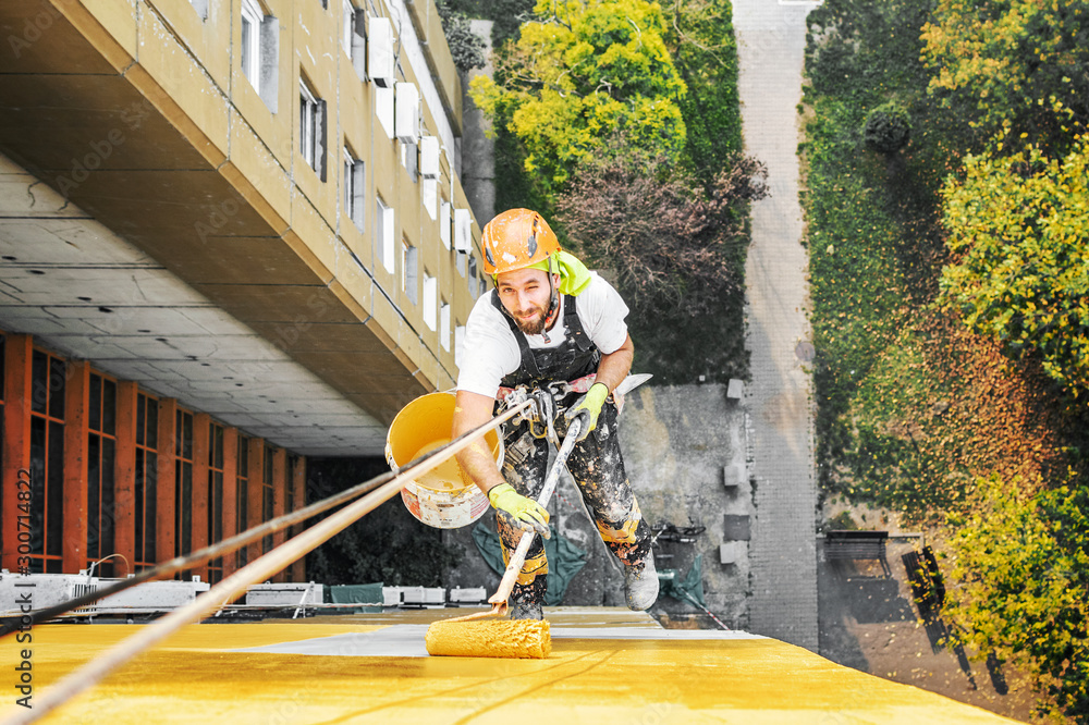 Industrial rope access worker hanging from the building while painting ...