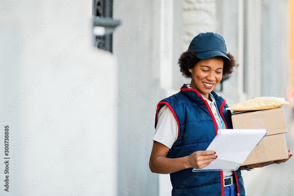 Happy African American mailwoman doing through check list while ...