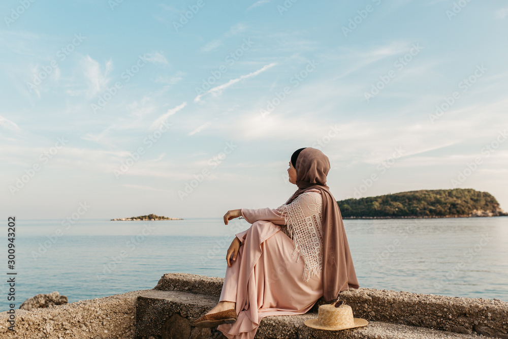 portrait of young European Muslim women with hijab sitting on the beach ...