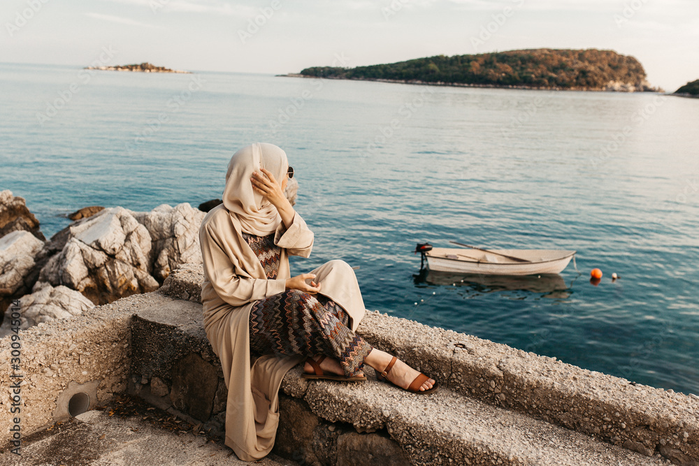 portrait of young European Muslim women with hijab sitting on the stone ...