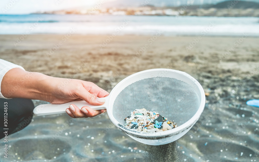 Young woman cleaning microplastics from sand on the beach ...
