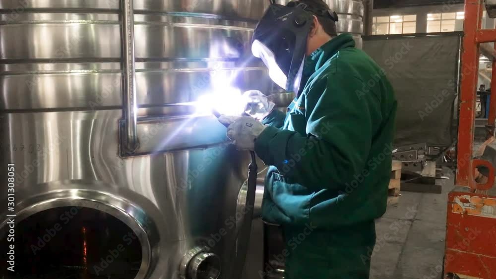 Worker welding stainless steel tank, using TIG, MIG welder, close up ...